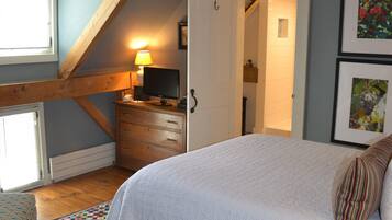 Quarto com teto de madeira, cama com colcha branca, cômoda, televisão e janela com persianas.