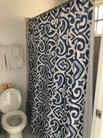 Casa de banho com cortina de chuveiro estampada, sanita e toalheiro com toalhas.