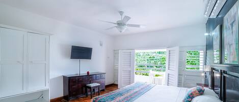 Quarto com cama, escrivaninha, cadeira, ventilador de teto e janela com persianas.
