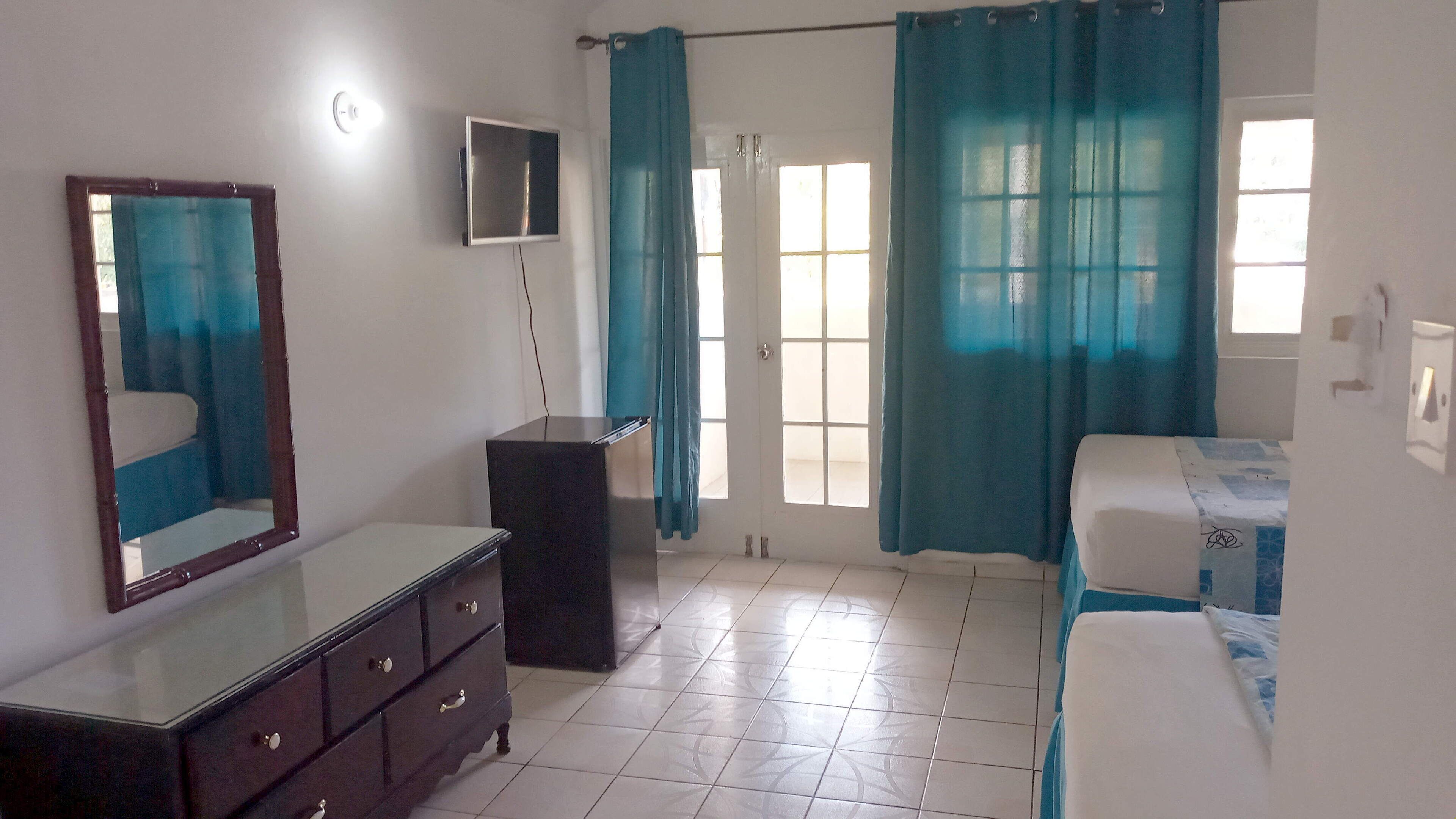 Quarto com cama, cómoda, televisão e janela com cortinas.