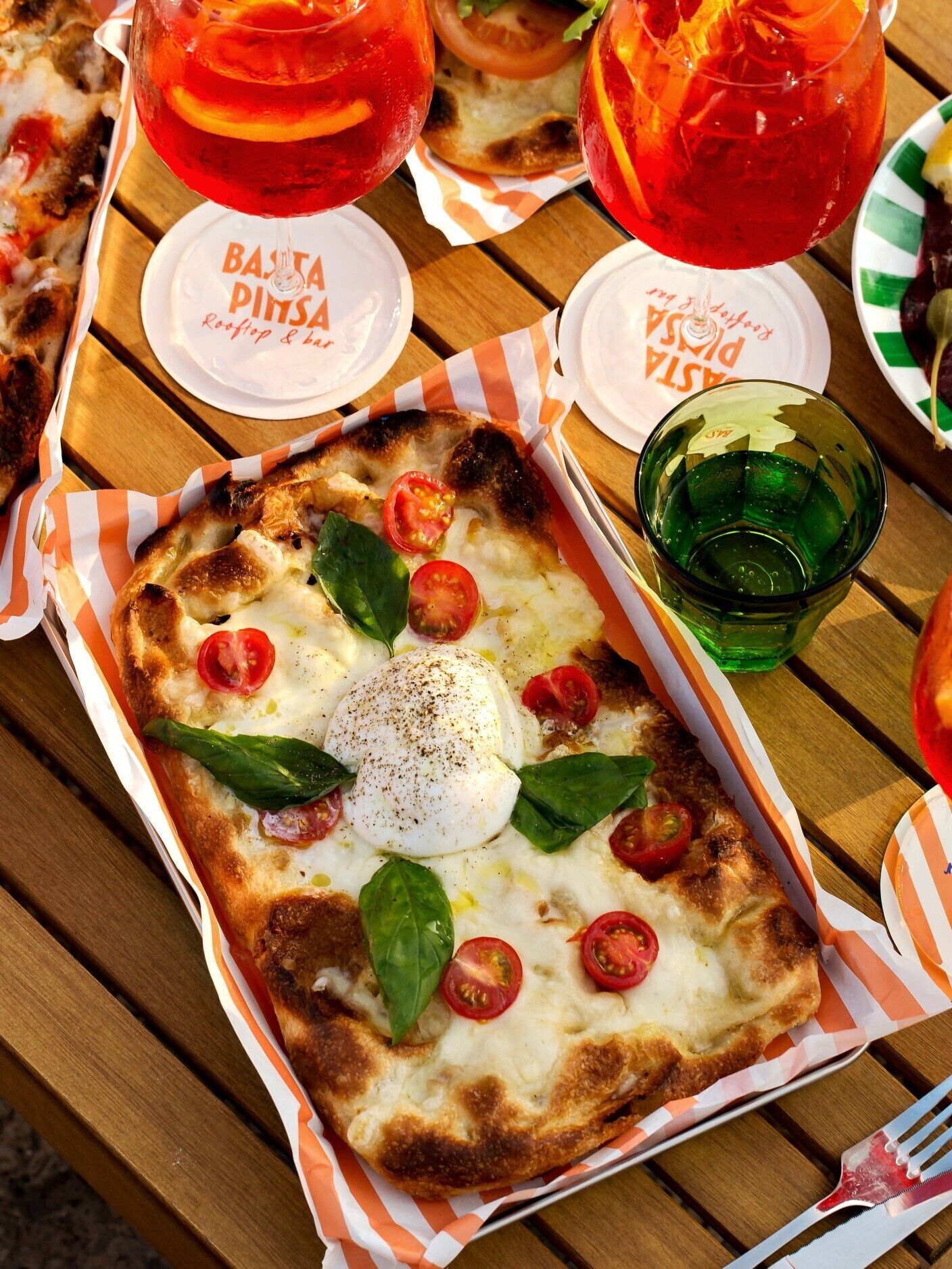 Pizza com cobertura e um copo de bebida vermelha sobre uma mesa de madeira.
