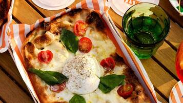 Pizza com cobertura e um copo de bebida vermelha sobre uma mesa de madeira.