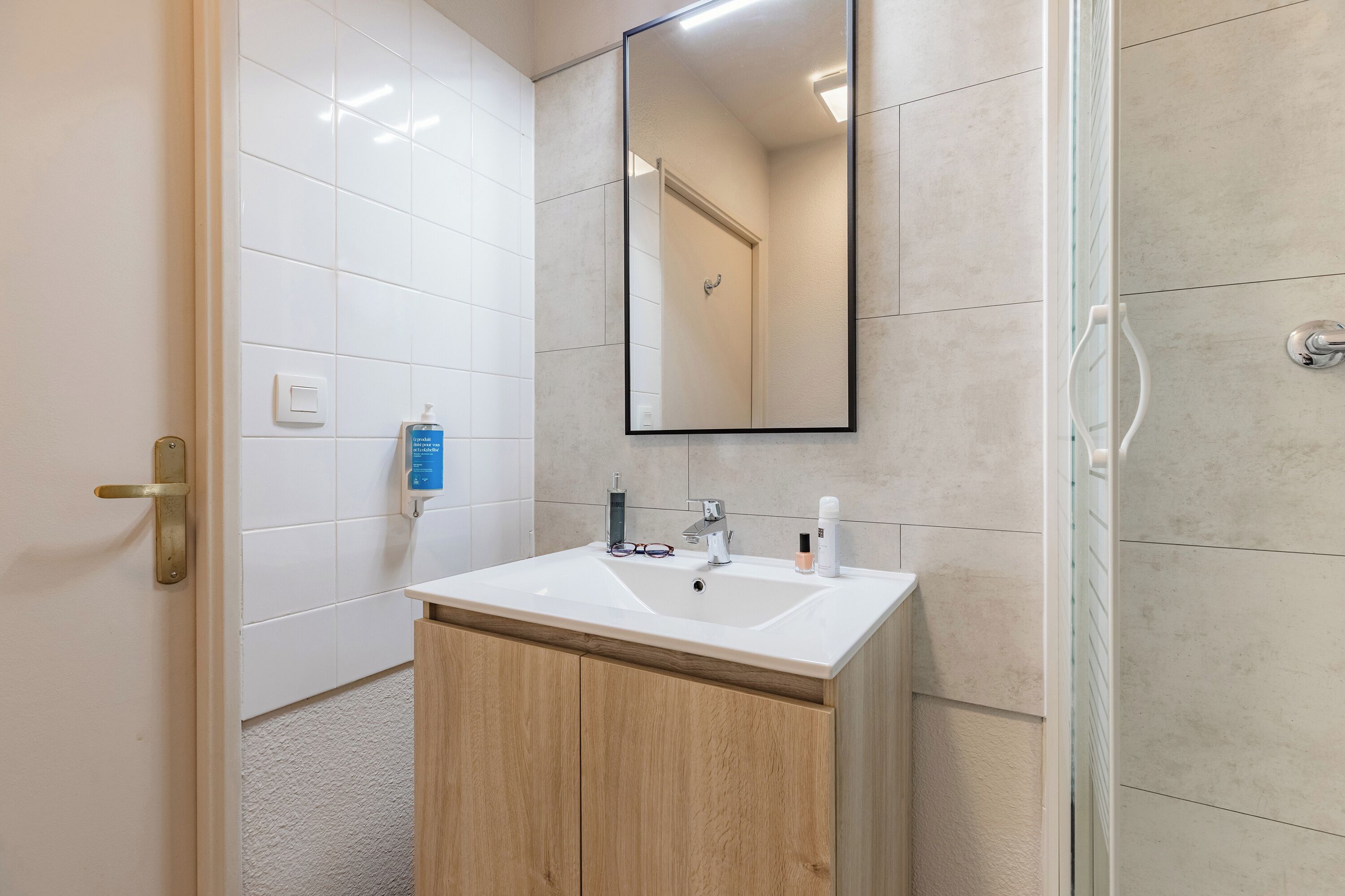 Casa de banho com lavatório branco, espelho e zona de duche.