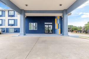 Entrada de um edifício com fachada azul, porta de vidro e área de estacionamento.