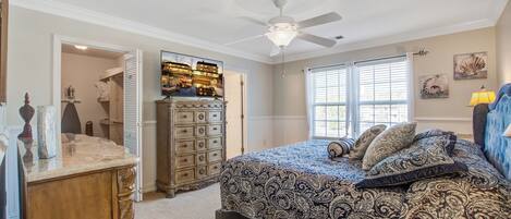 Quarto com cama, cômoda, televisão e ventilador de teto.
