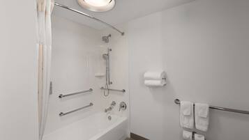 Casa de banho moderna com banheira, chuveiro, barras de apoio, porta-toalhas e suporte para papel higiénico.