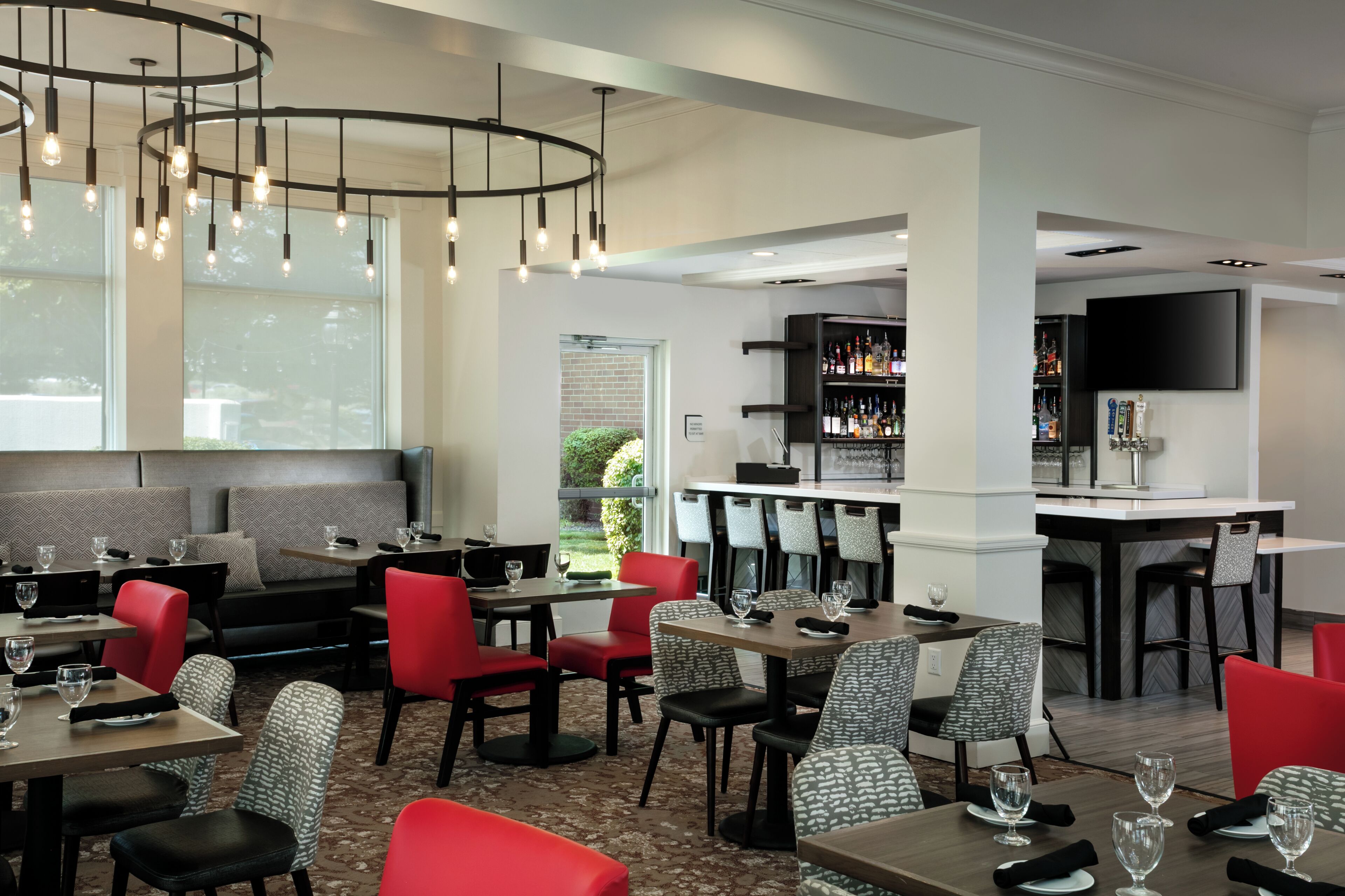 Interior moderno de restaurante com área de bar, mesas e cadeiras, e uma tela de televisão.