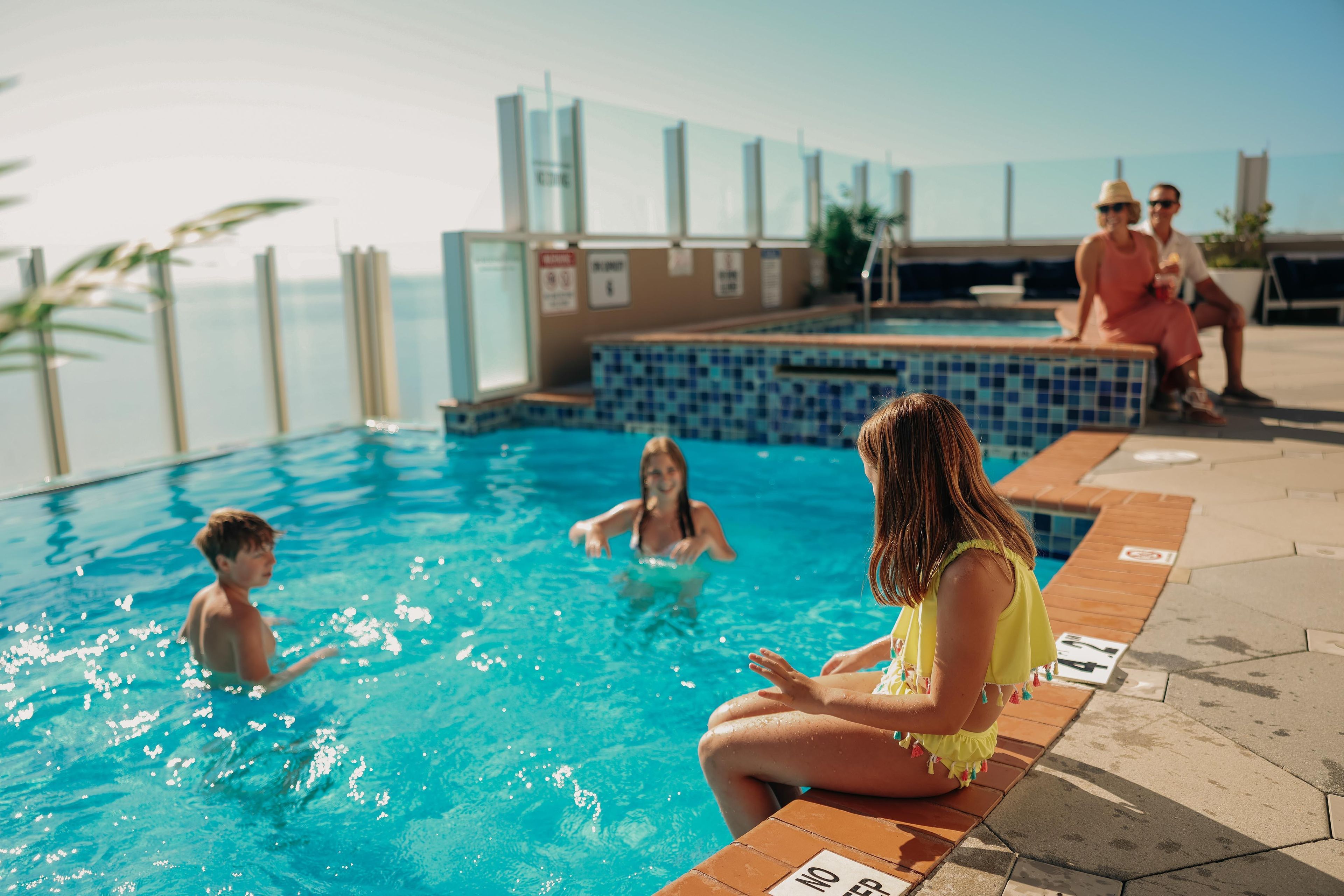 Piscina com borda azulejada, superfície de água azul cristalina e vista para o mar ao fundo.