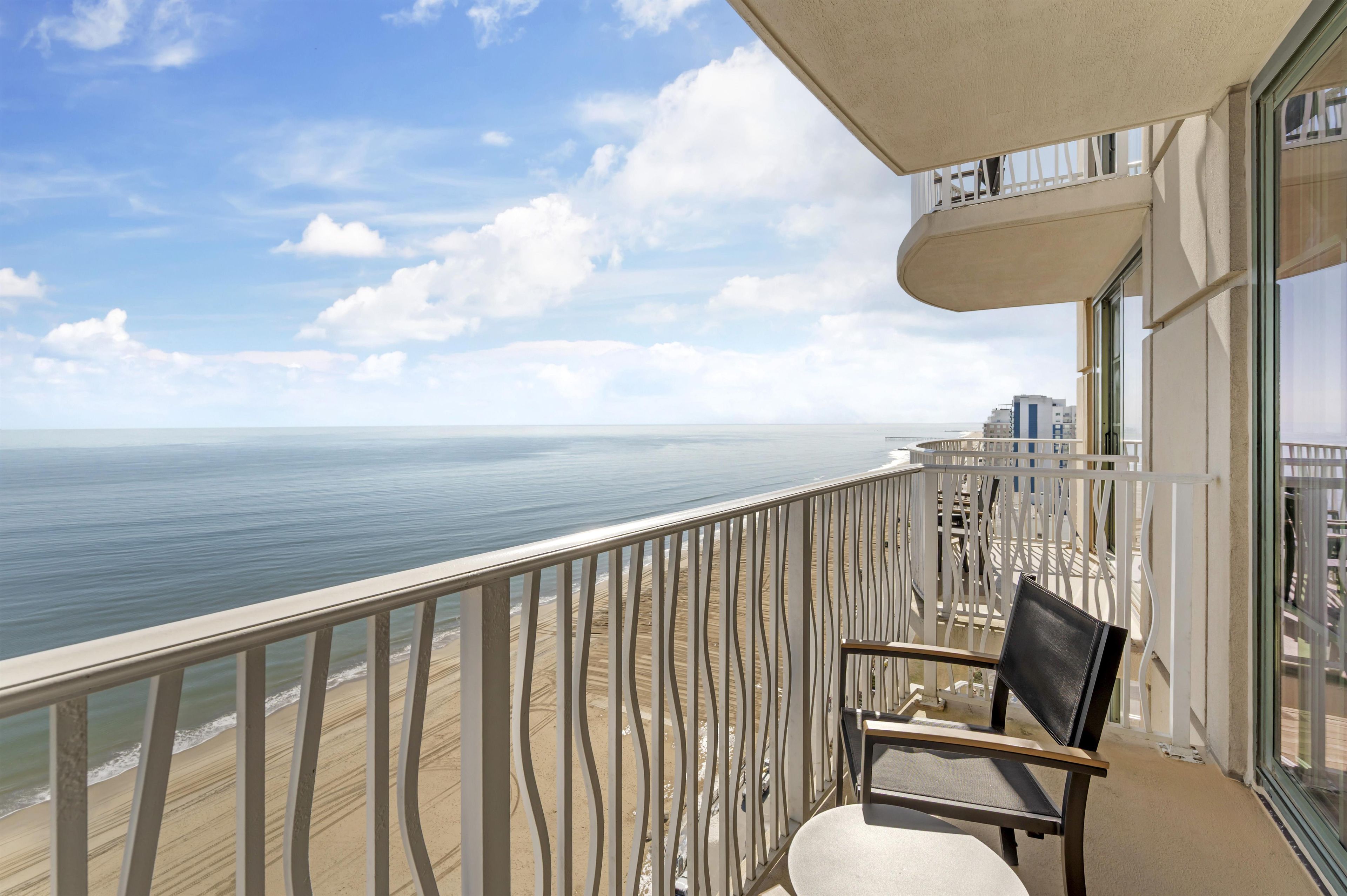 Varanda com vista para o mar, uma cadeira e um prédio ao fundo.