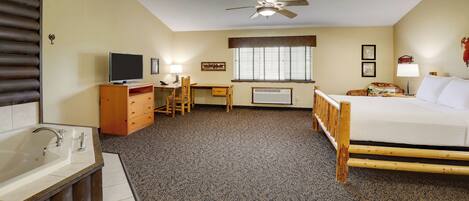 Quarto de hotel com uma cama grande, uma escrivaninha, uma cadeira, uma televisão, banheiro com banheira e um ventilador de teto.