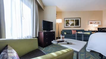 Quarto de hotel com cama, sofá, mesa de centro, televisão em uma cômoda e abajur.