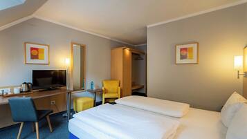 Quarto de hotel com cama, escrivaninha com televisão, cadeira e guarda-roupa.