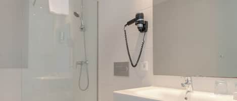 Casa de banho moderna com chuveiro envidraçado, lavatório branco e secador de cabelo fixado na parede.