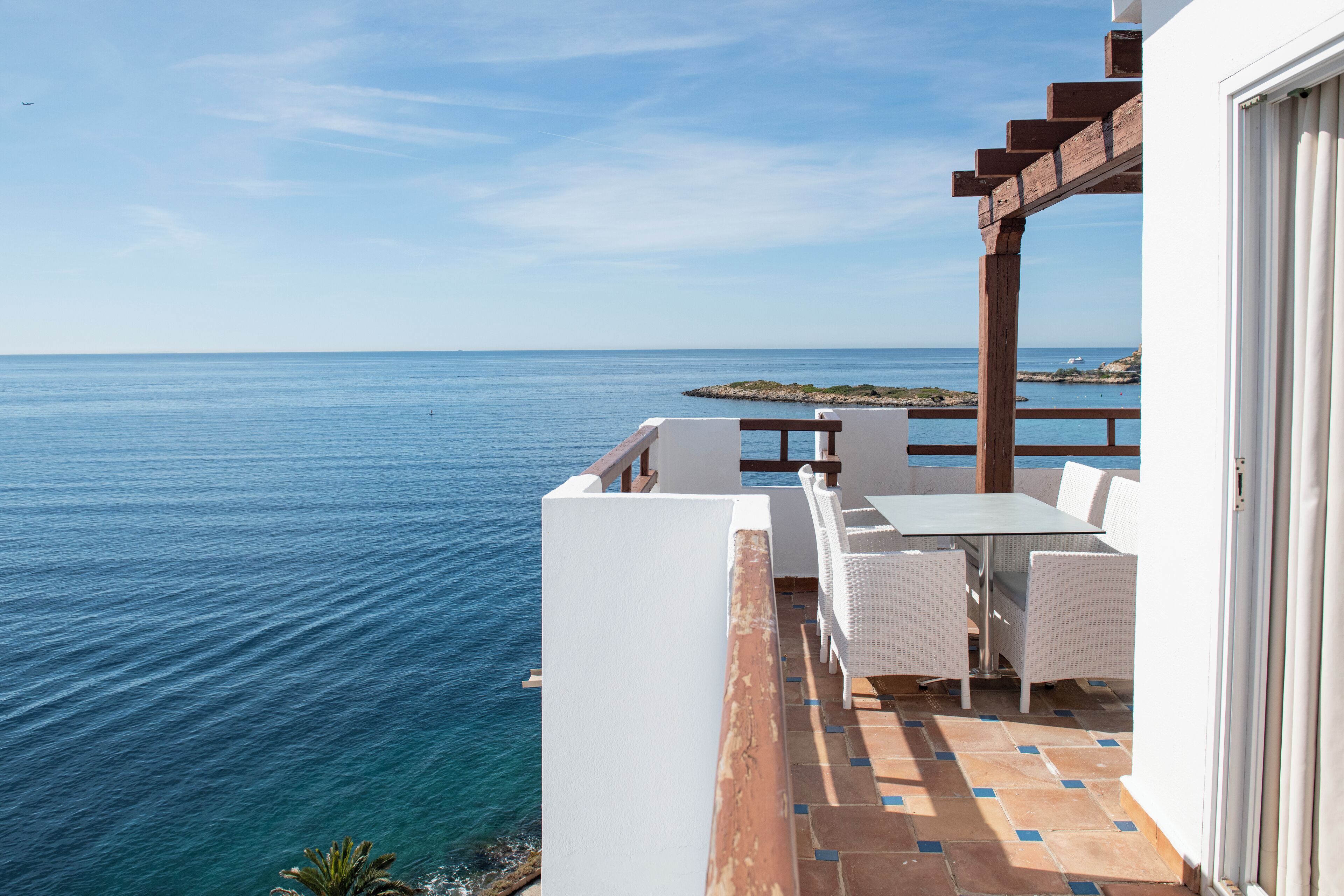 Terraço com vista para o mar, mobiliário de vime branco e pérgola de madeira.