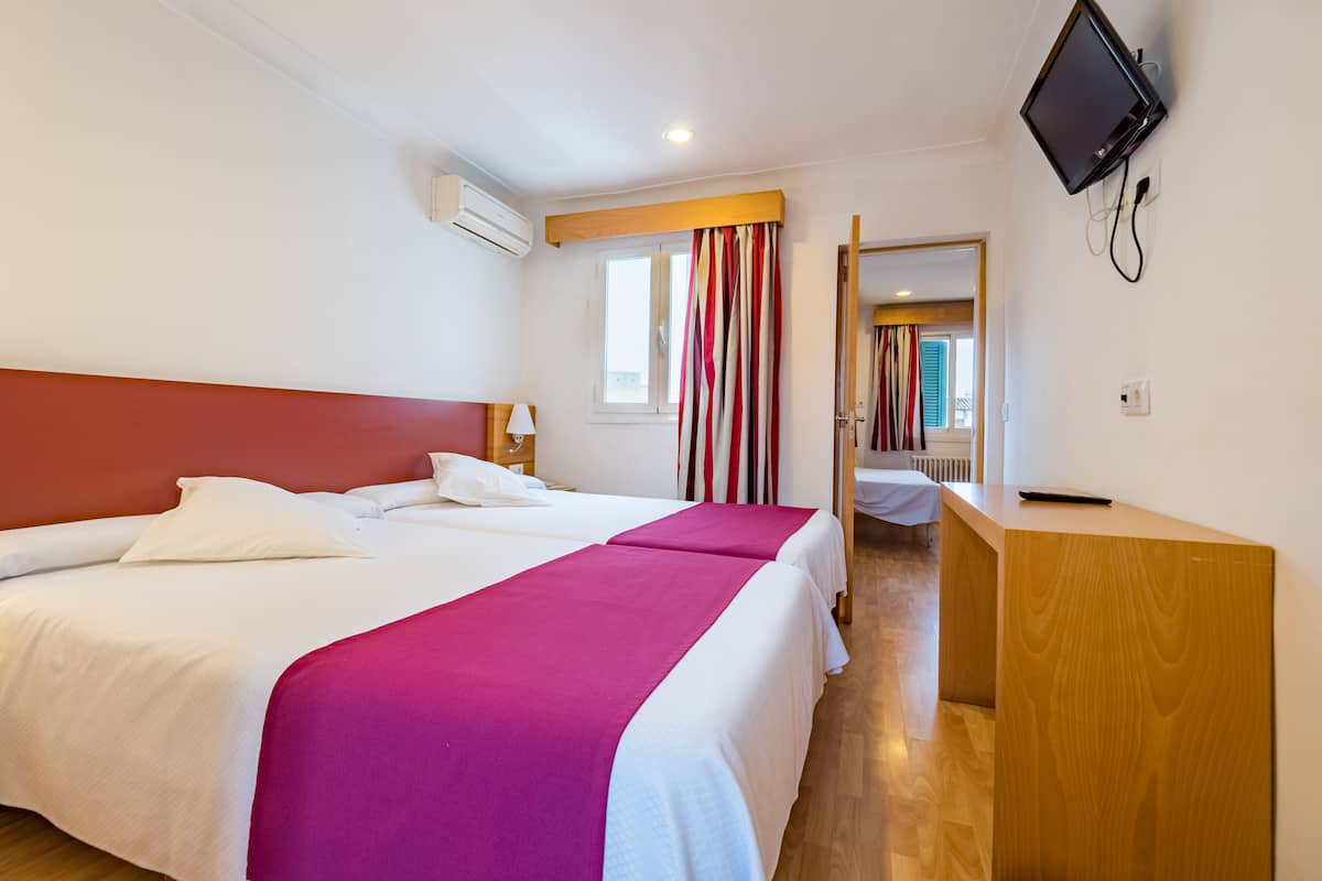 Quarto de hotel com duas camas, uma escrivaninha, uma televisão e uma janela com cortinas.
