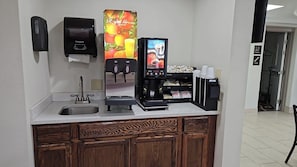 Uma estação de bebidas de serviço, com uma máquina de café, um dispensador de suco e um refrigerador.