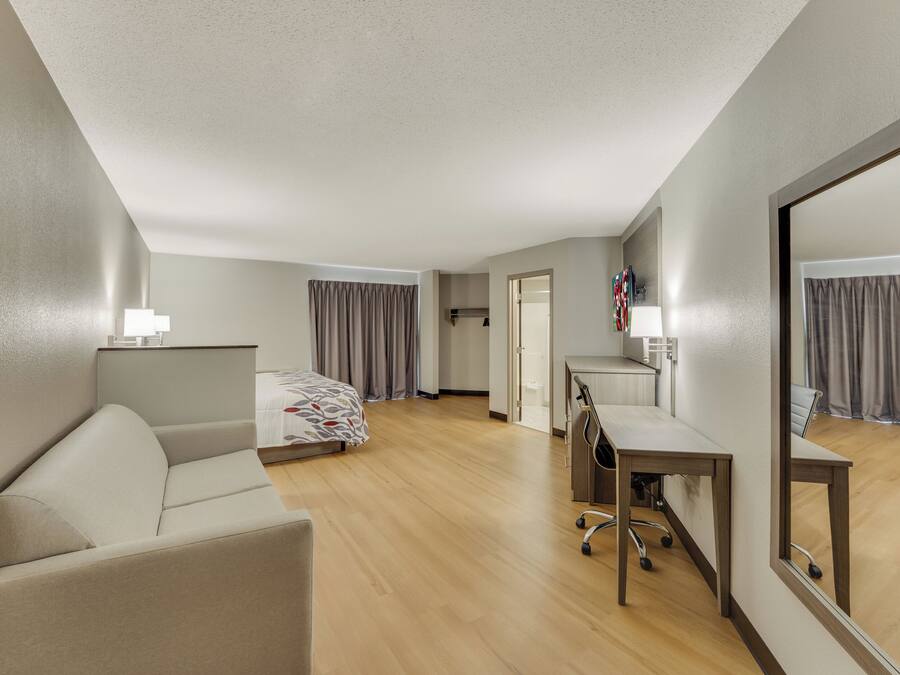 Quarto de hotel com cama, escrivaninha, cadeira, espelho e luminária.