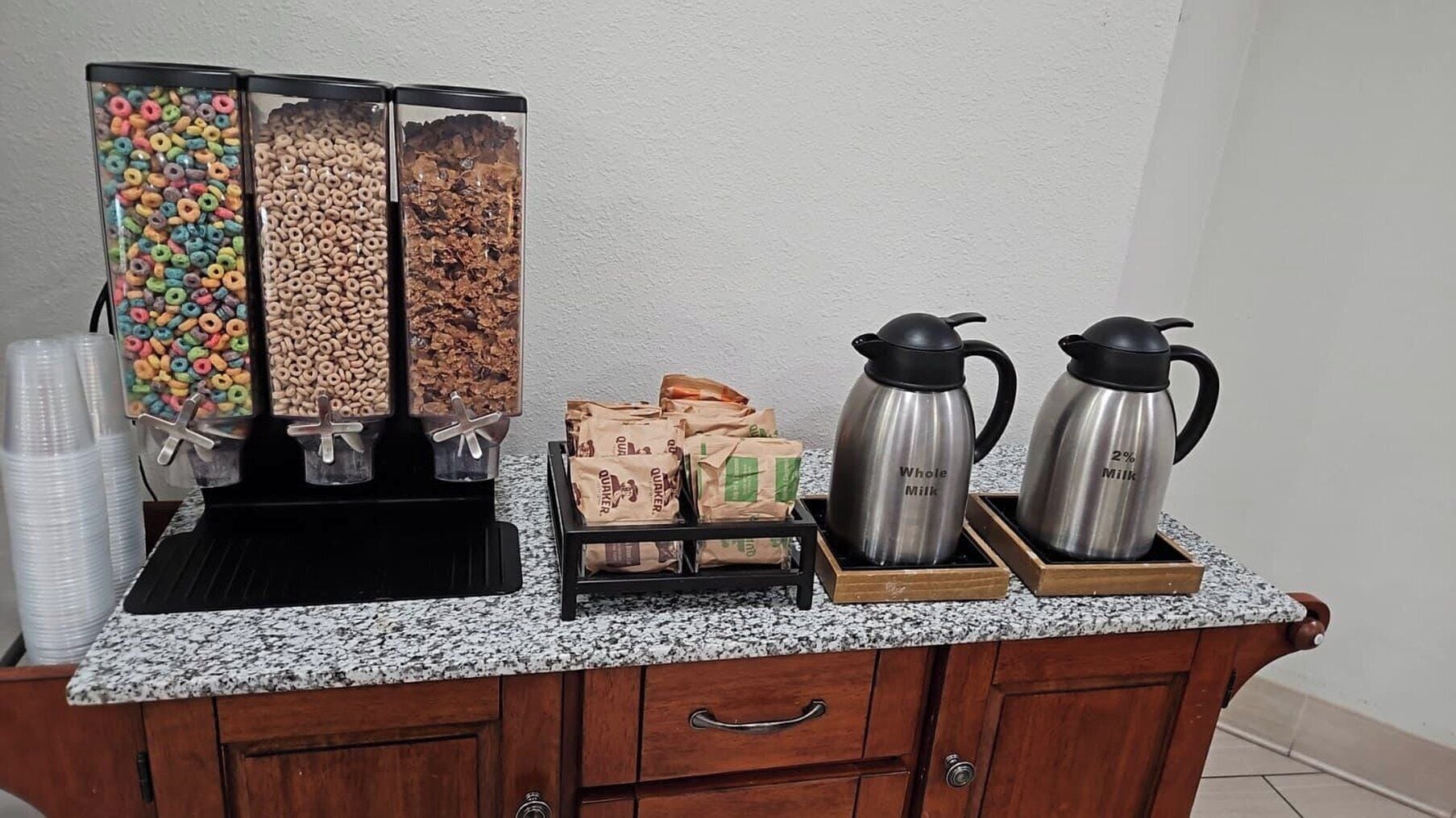 Um balcão de café da manhã com distribuidores de cereais, jarras de café e embalagens de Quaker Oats.