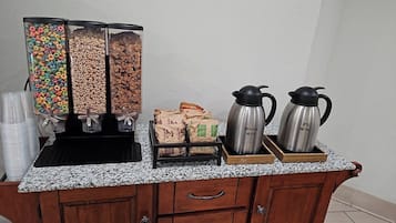 Um balcão de café da manhã com distribuidores de cereais, jarras de café e embalagens de Quaker Oats.
