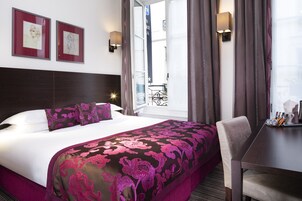 Quarto de hotel com uma cama grande, uma mesa de jantar e duas obras de arte emolduradas na parede.