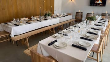 Uma longa mesa de jantar posta com toalhas brancas, bancos de madeira e velas.
