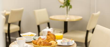 Mesa redonda com croissants, café, sumo de laranja e um vaso de flores para o pequeno-almoço.
