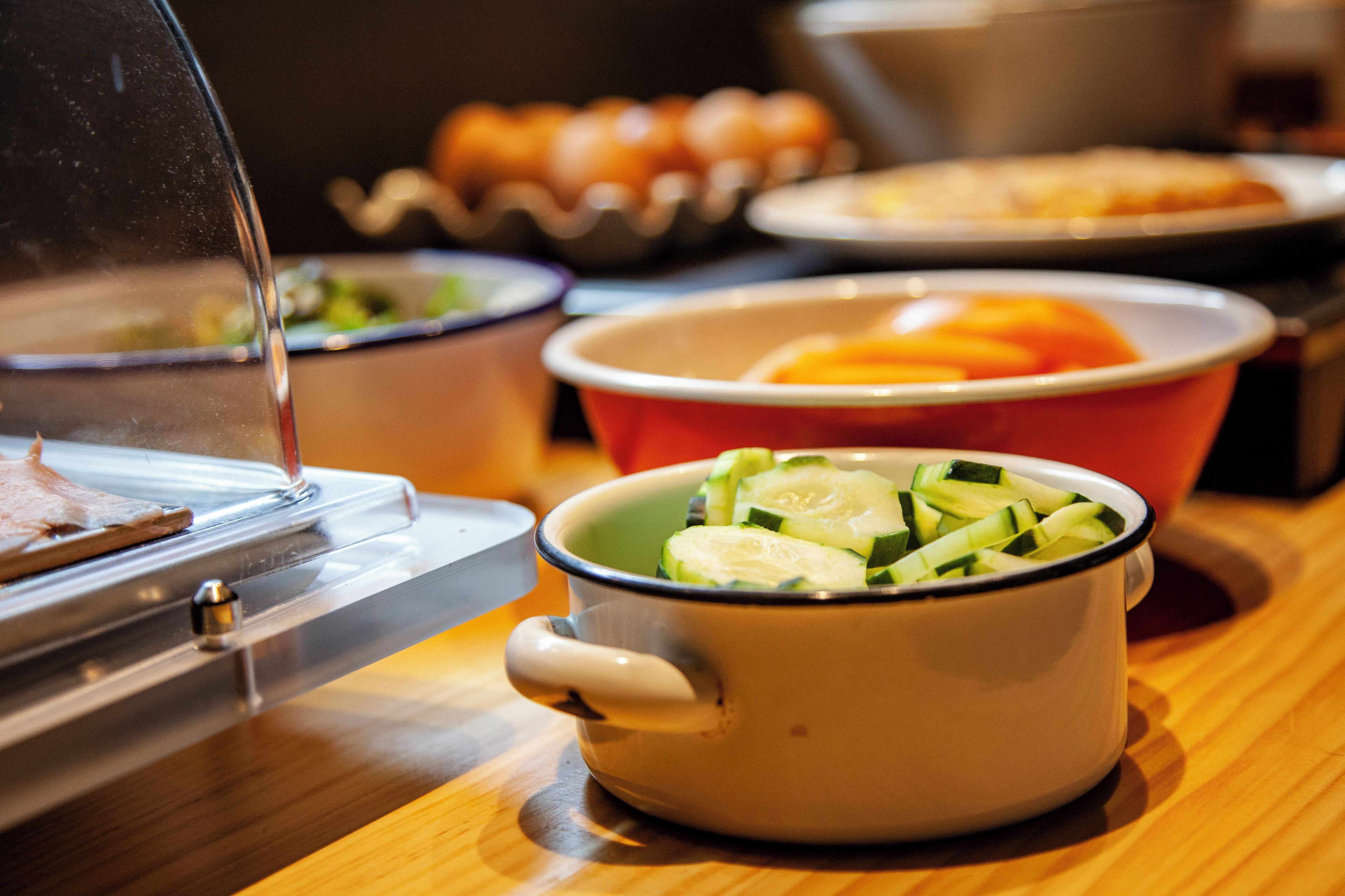 Mesa de buffet com diversos pratos, incluindo uma tigela de pepinos fatiados e uma tigela de fatias de laranja.