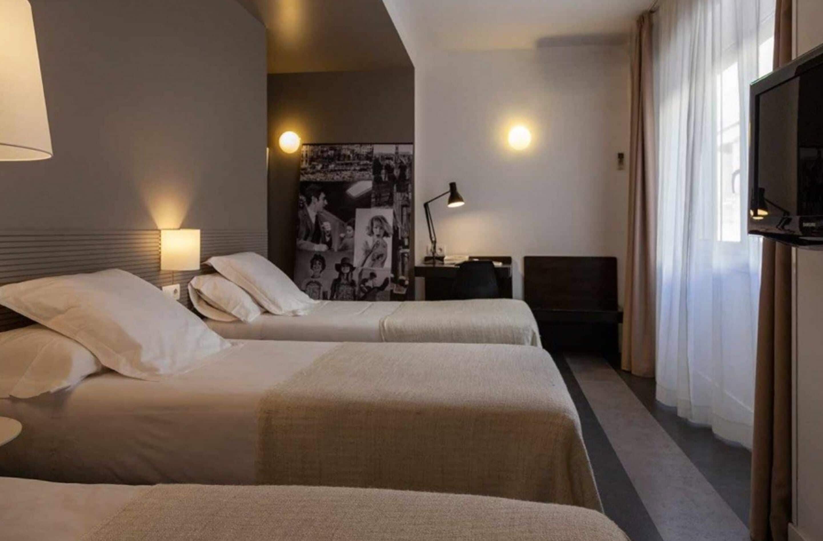 Quarto de hotel com duas camas, televisão, escrivaninha e parede com um cartaz.