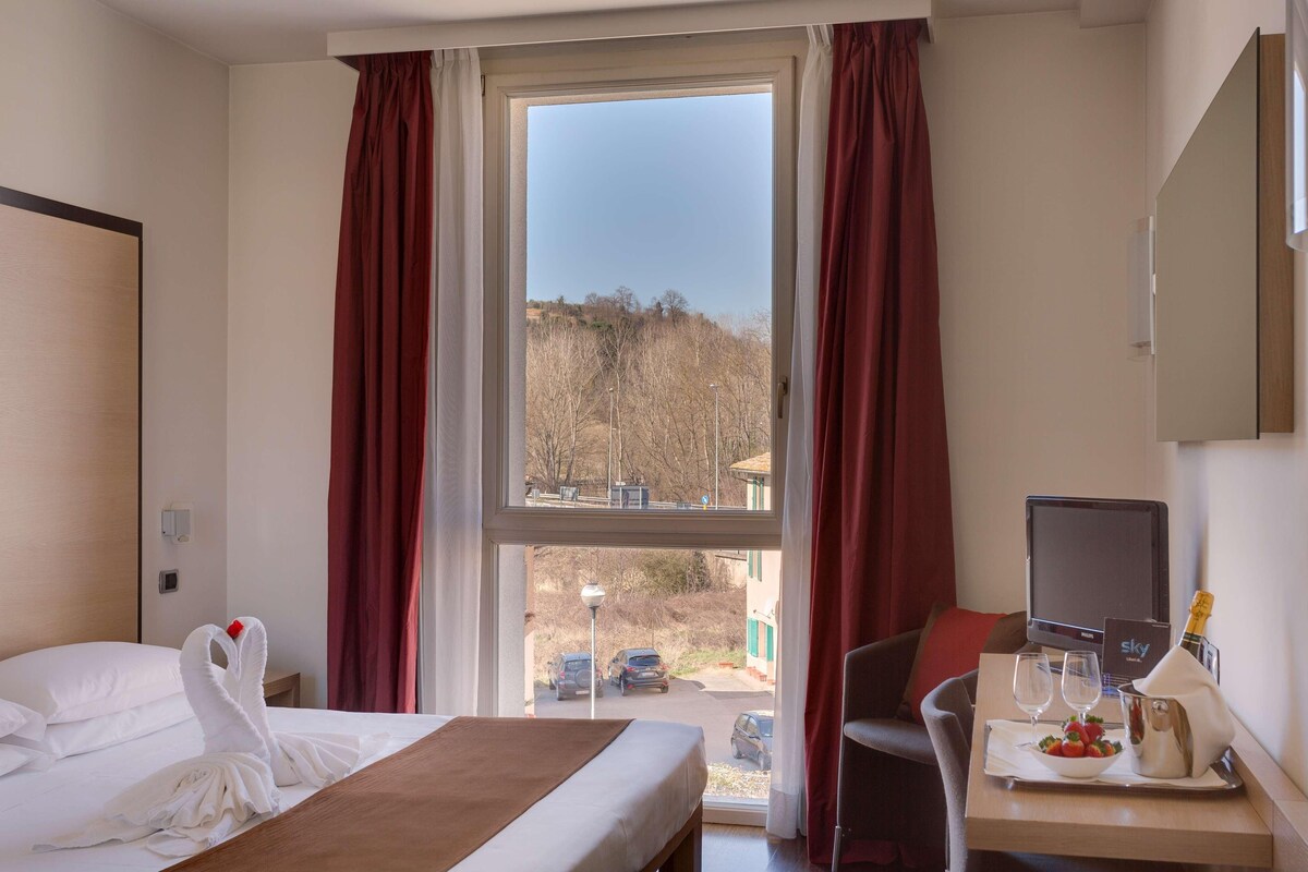 Quarto de hotel com uma cama, uma mesa com computador, uma garrafa de champanhe e vista para o exterior.