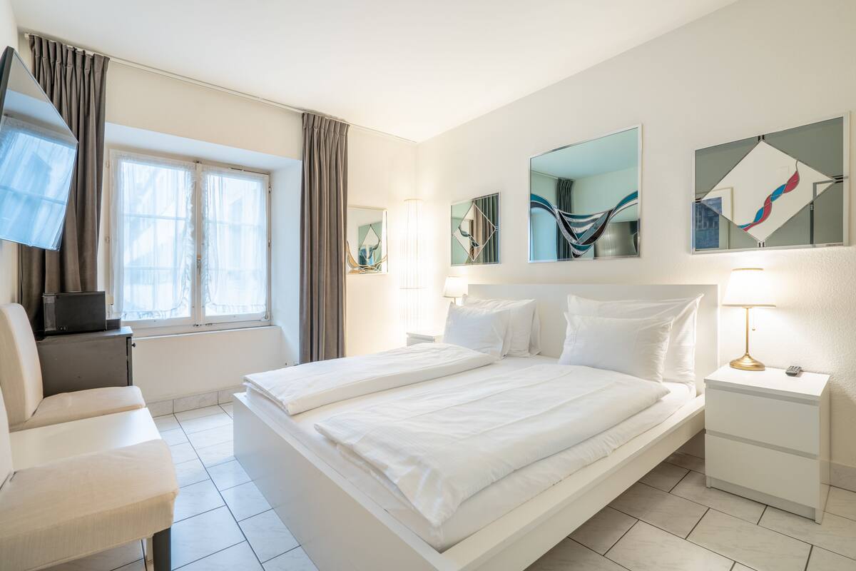 Quarto de hotel com cama, mesas de cabeceira, escrivaninha e uma cadeira.