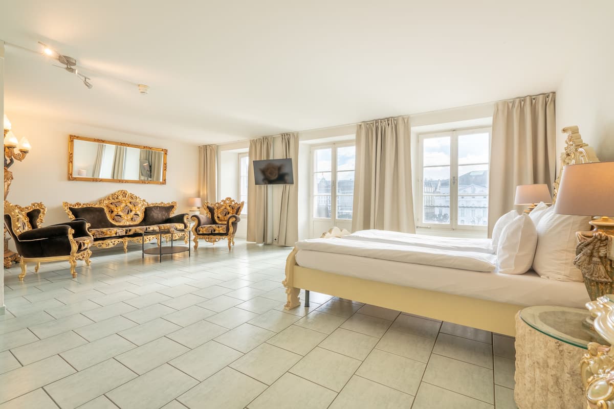 Quarto espaçoso com uma cama grande, um conjunto de sofás, uma TV e vista para a cidade.