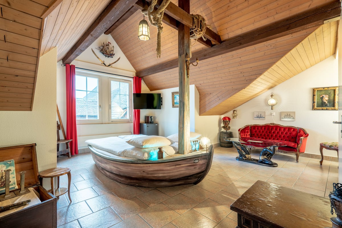 Um quarto com cama em formato de barco, vigas de madeira, um sofá vermelho e uma televisão.