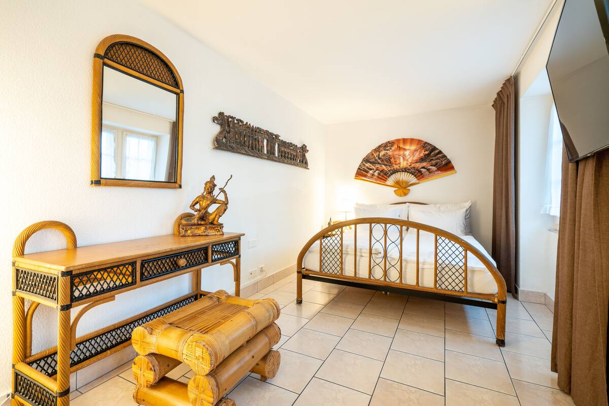 Um quarto com uma cama, uma mesa de madeira, um banco, um espelho e uma decoração na parede.