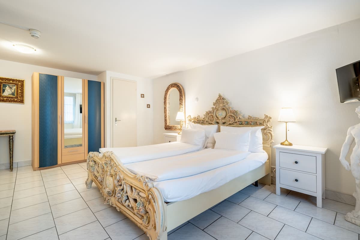 Uma cama de casal com cabeceira decorada, uma mesa de cabeceira com abajur e um espelho grande na parede.