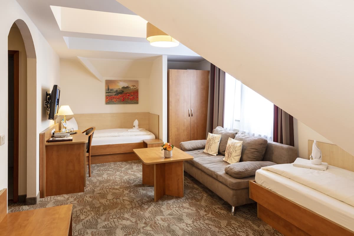 Quarto de hotel moderno com cama beliche, sofá, pequena mesa e escrivaninha.