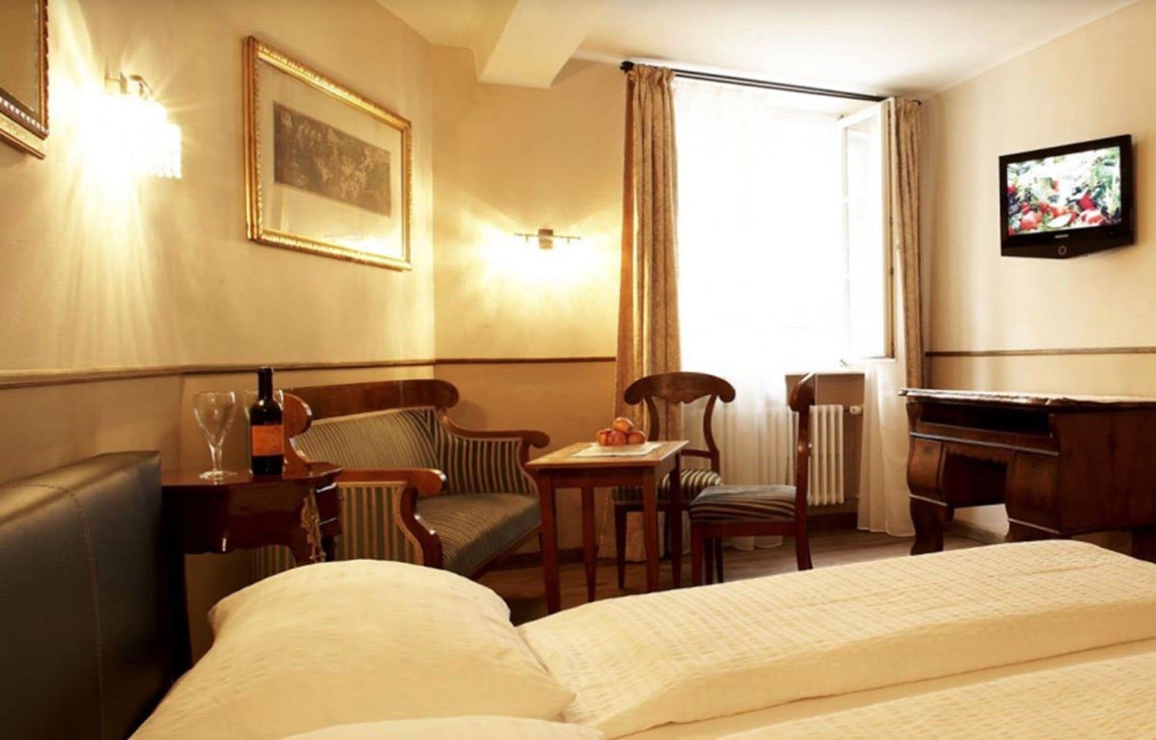 Quarto de hotel com cama, escrivaninha, cadeira, televisão e janela com cortinas.