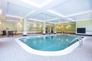 Piscina interna com água cristalina, cercada por piso e paredes revestidas, com teto com iluminação embutida e um corrimão visível.