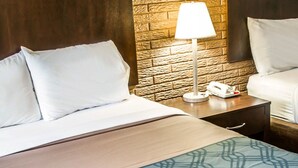 Quarto de hotel com uma cama, mesa de cabeceira com abajur e telefone.