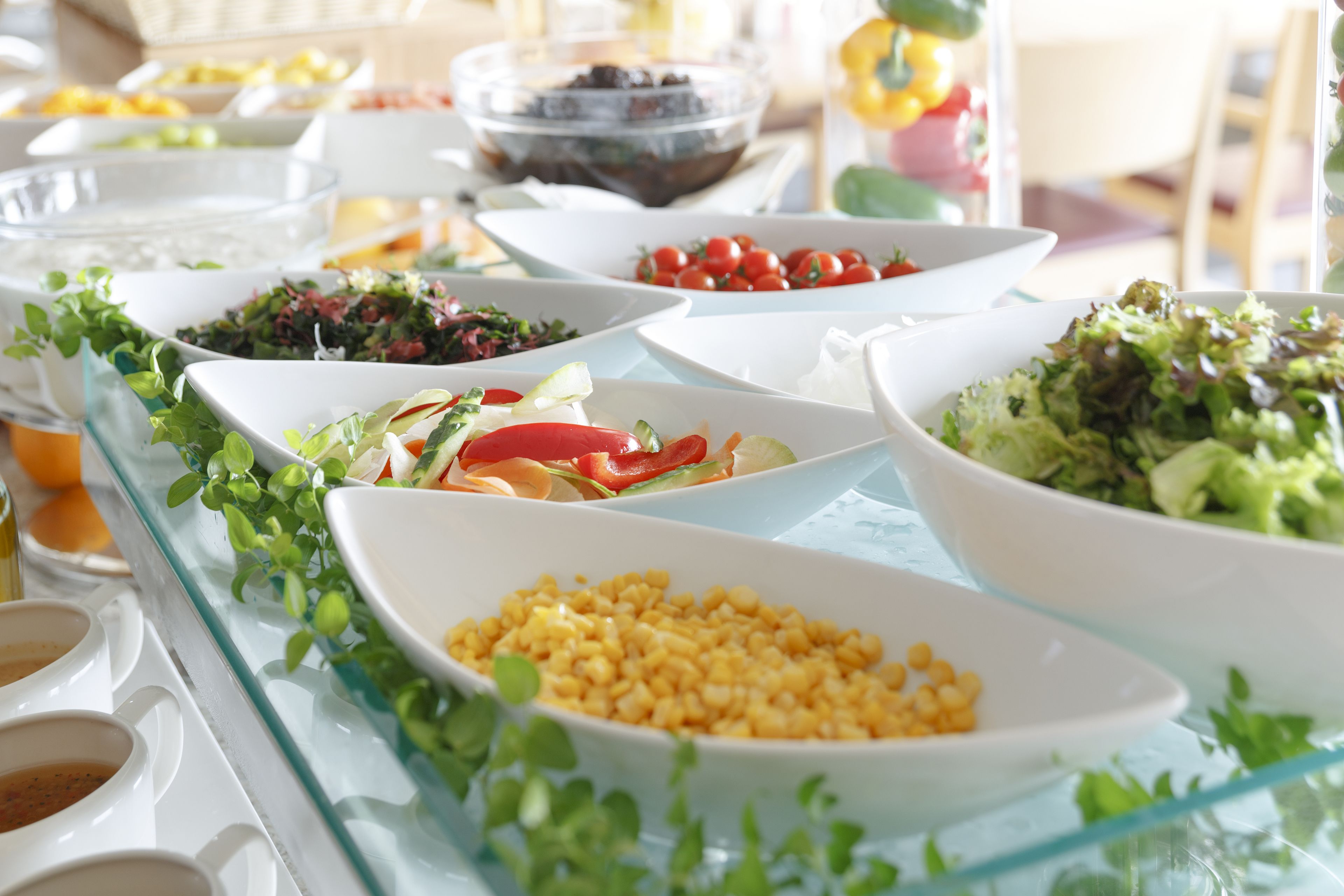 Uma mesa de buffet com diversos pratos, incluindo saladas, legumes e milho.