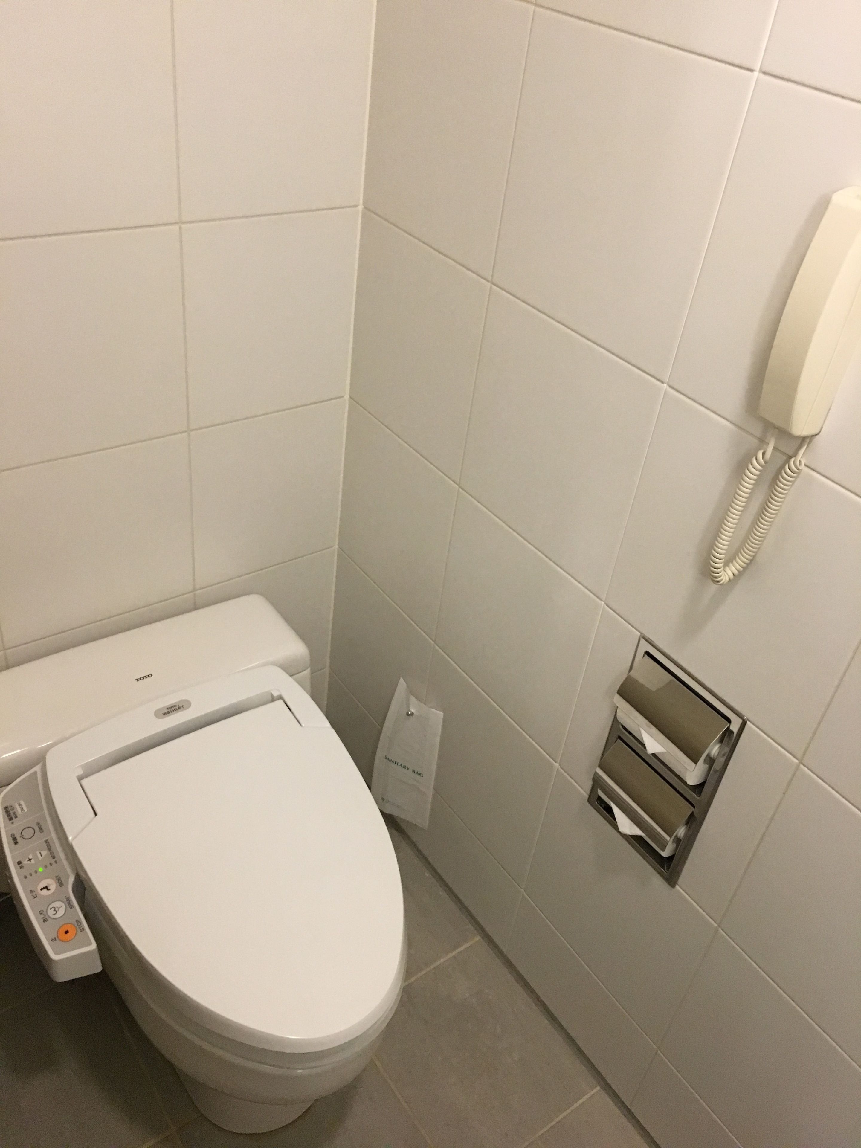 Uma casa de banho moderna com sanita, secador de mãos e dispensador de papel.