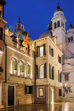Um edifício histórico com janelas em arco e uma varanda, ao lado de uma igreja com torres em cúpula.