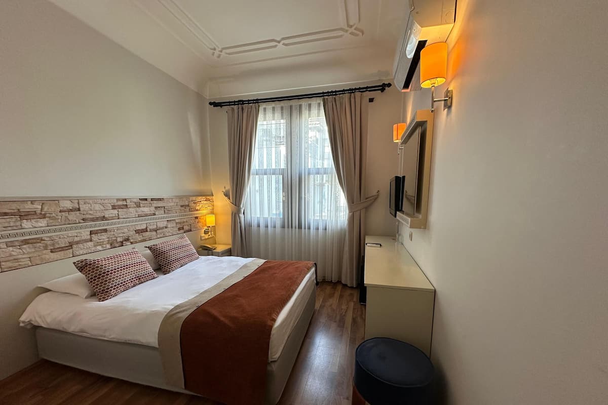 Quarto de hotel com cama, mesa de cabeceira com abajur, espelho e um banquinho.