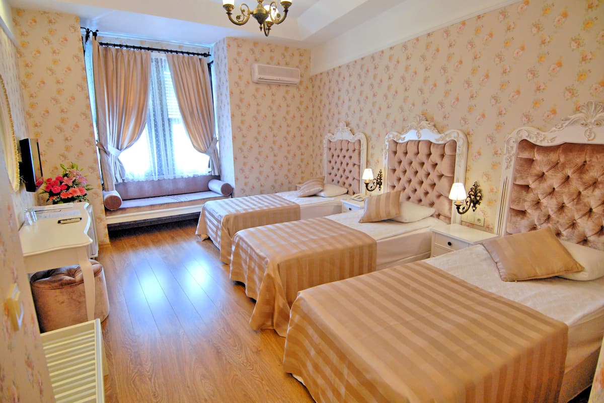 Quarto de hotel com duas camas, uma toucador com espelho, mesa de cabeceira com abajur e janela com cortinas.