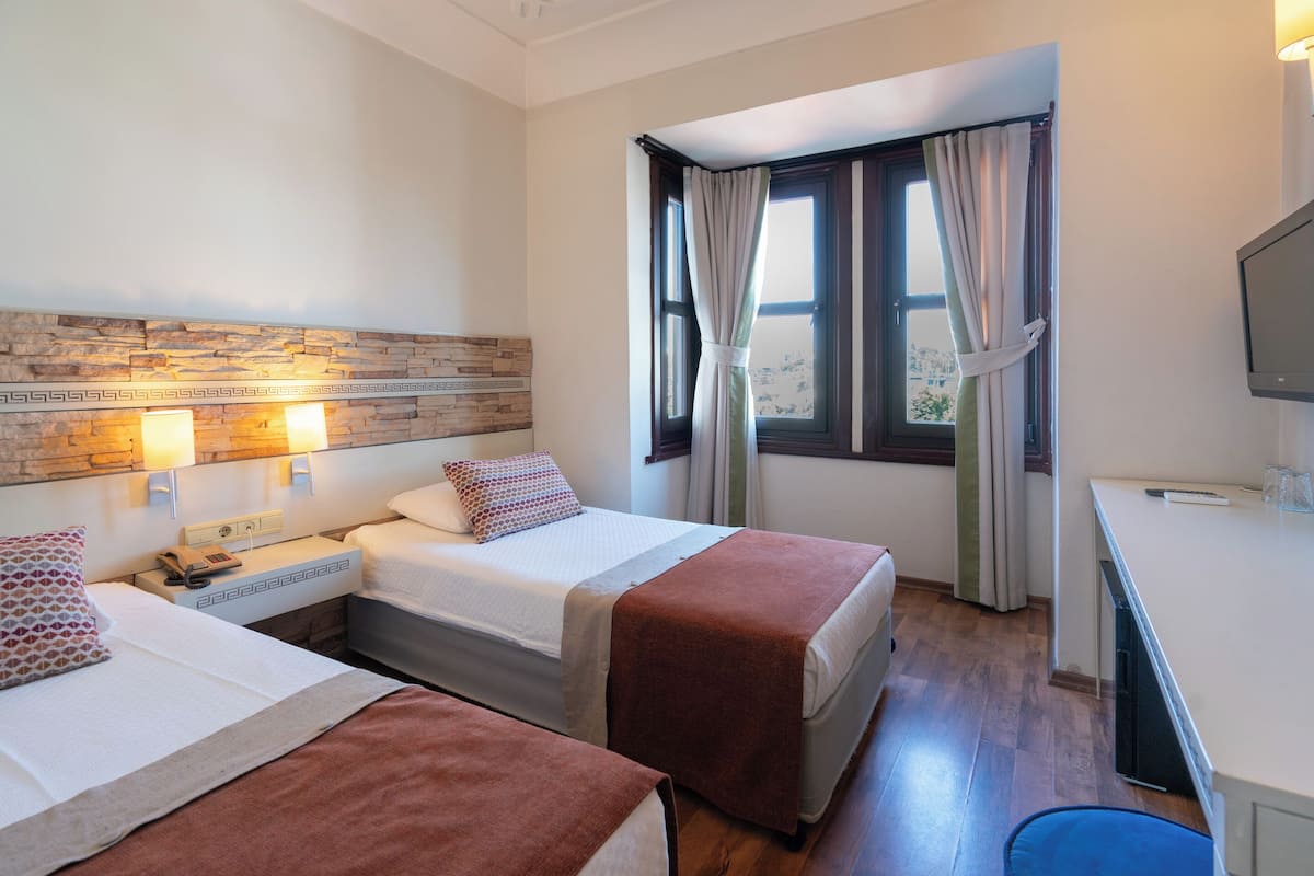 Quarto de hotel com duas camas, parede de destaque em pedra, televisão de tela plana e janela com cortinas.