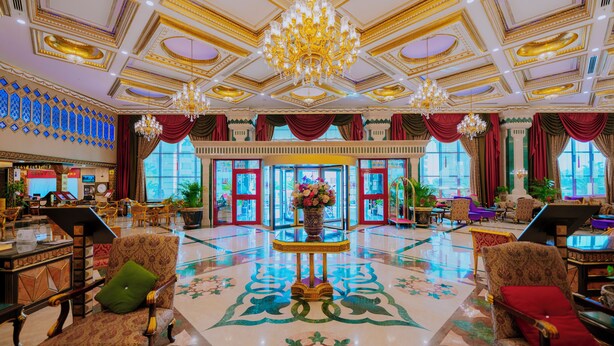 Um lobby luxuoso com lustres elaborados, pisos com mosaicos e áreas de estar confortáveis.