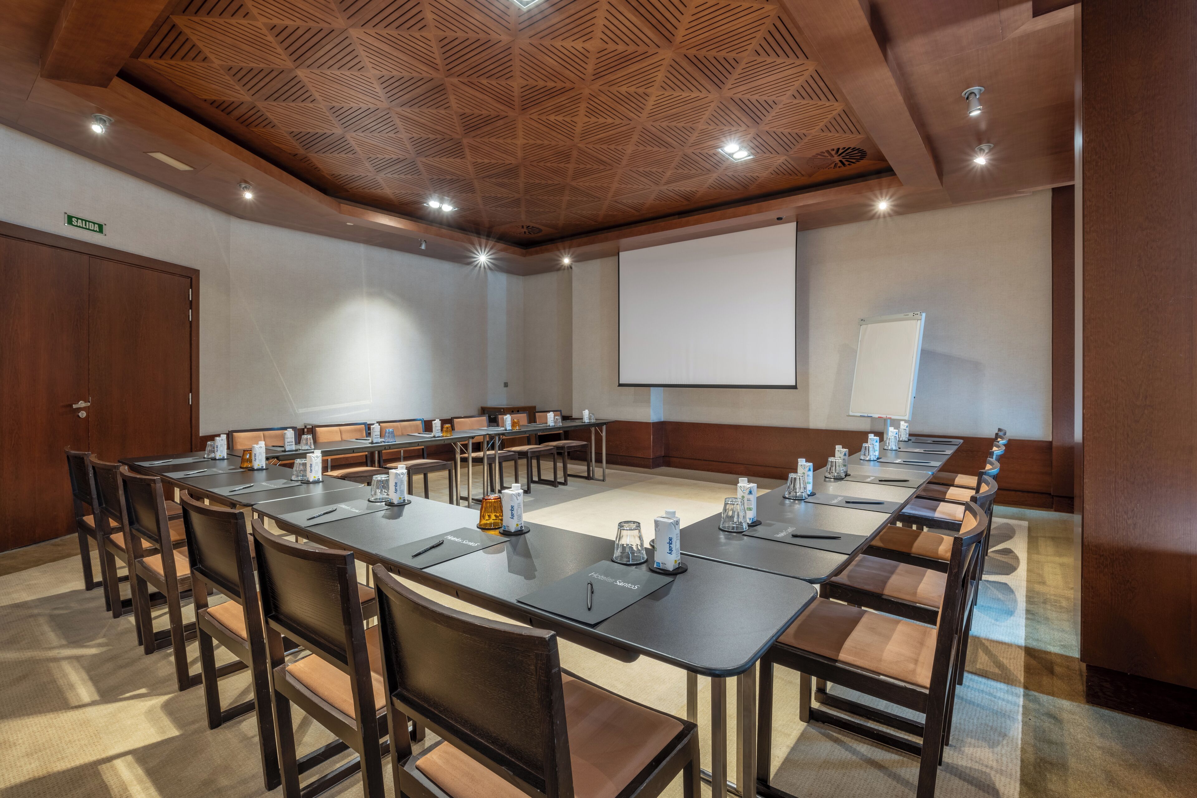 Uma sala de conferência com uma mesa comprida, cadeiras, uma tela de projetor e um quadro branco.
