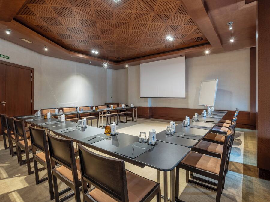Uma sala de conferência com uma mesa comprida, cadeiras, uma tela de projetor e um quadro branco.