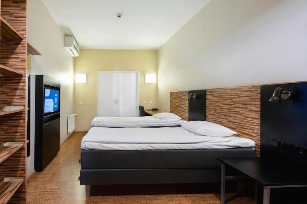 Quarto de hotel com cama, televisão, guarda-roupa e escrivaninha.