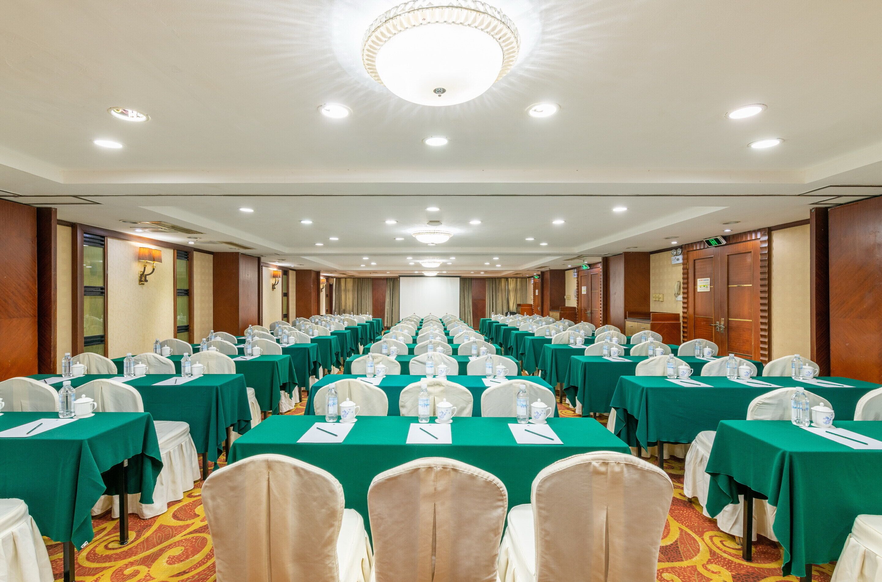 Uma sala de conferências com fileiras de mesas, cadeiras e um candelabro.
