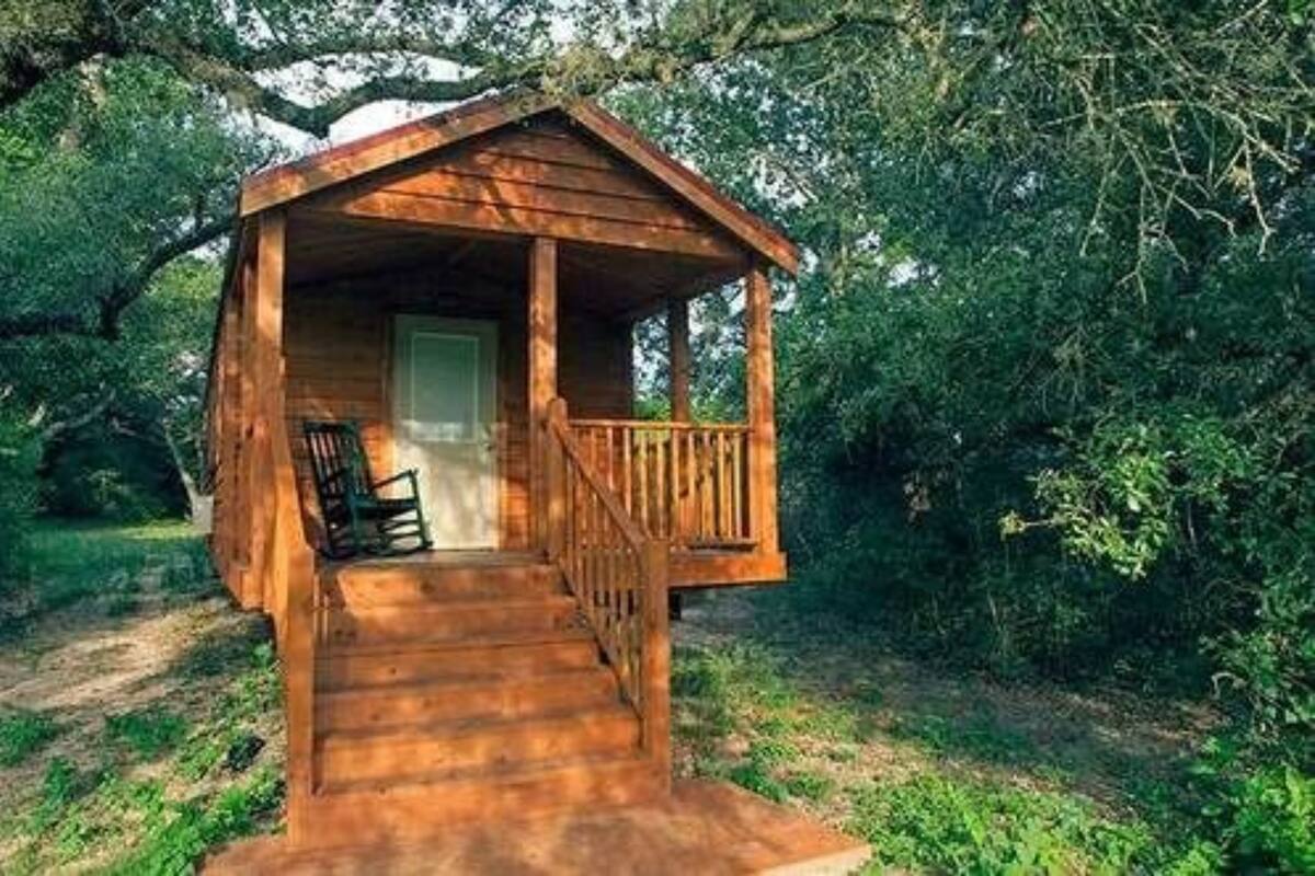 Uma cabana de madeira com varanda e degraus que levam à porta.